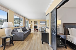 Quarto de hotel com sofá, mesa pequena com luminária, cama, cômoda e uma grande janela com vista para o exterior.