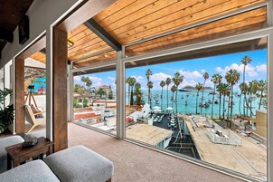 Quarto com grande janela vista para uma marina com barcos e palmeiras.