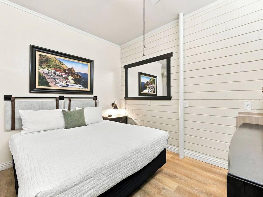Quarto com cama, mesa de cabeceira, abajur, cômoda e duas quadros na parede.