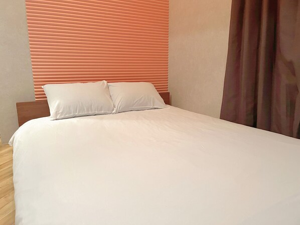 Cama com roupa de cama branca e duas almofadas, cabeceira de madeira e parede laranja listrada ao fundo.