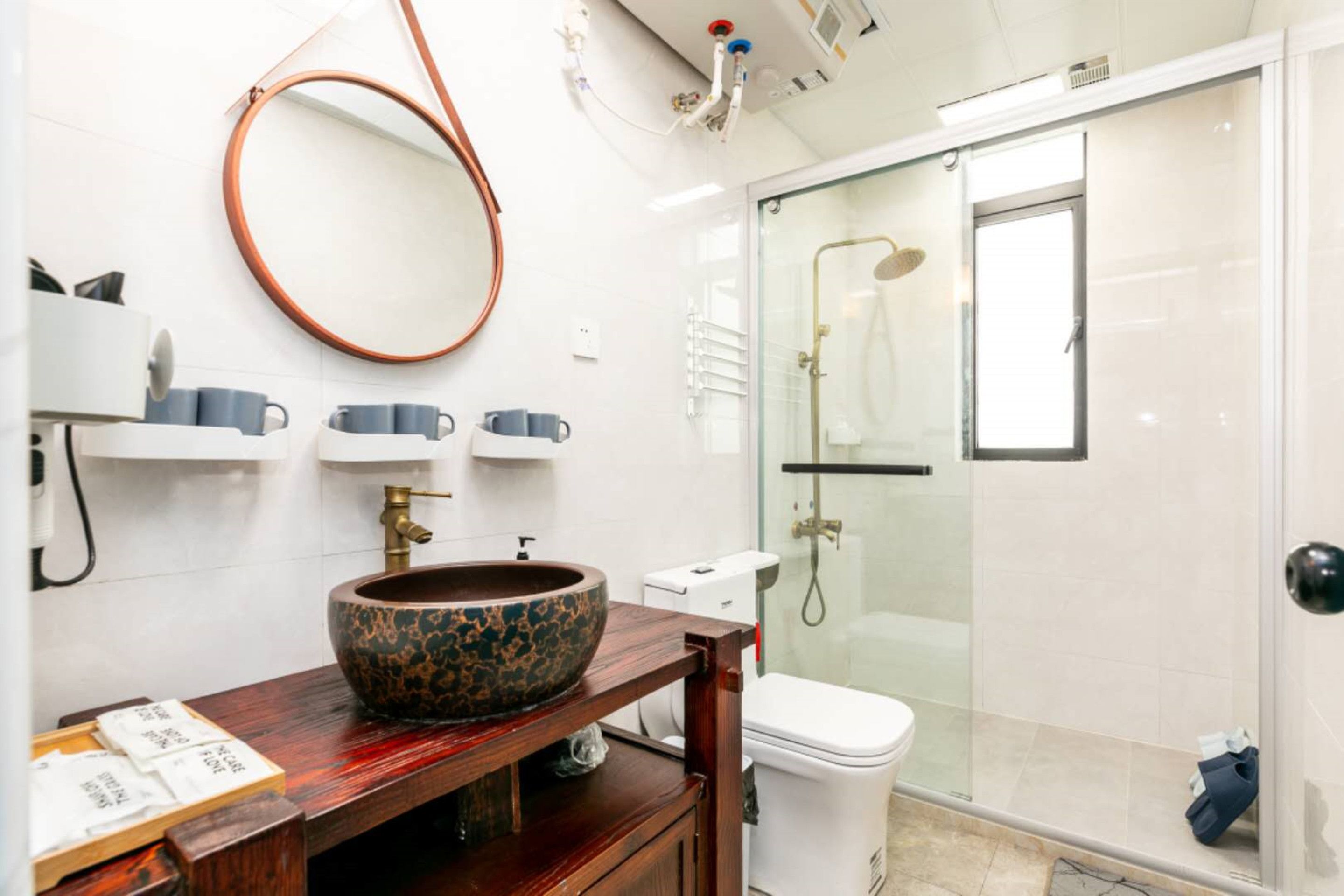 Um banheiro moderno com uma pia grande e decorativa, um box de vidro e um espelho redondo.