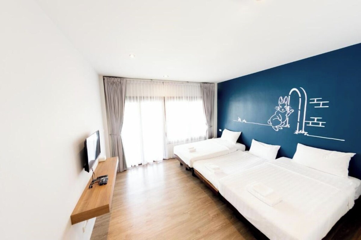 Quarto de hotel com uma cama grande, televisão em um suporte e uma parede azul com um detalhe gráfico.