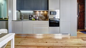 Uma cozinha moderna com armários cinzentos, micro-ondas embutido e forno. Há uma mesa de jantar de madeira em primeiro plano.