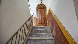 Uma escadaria com uma porta de madeira no topo, corrimão de metal e uma luminária decorativa no teto.
