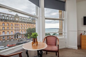 Quarto com uma janela ampla que dá para um edifício histórico e vista para o mar.