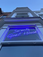Um letreiro de neon com a inscrição 'Serenity Guest House' na fachada de um edifício.