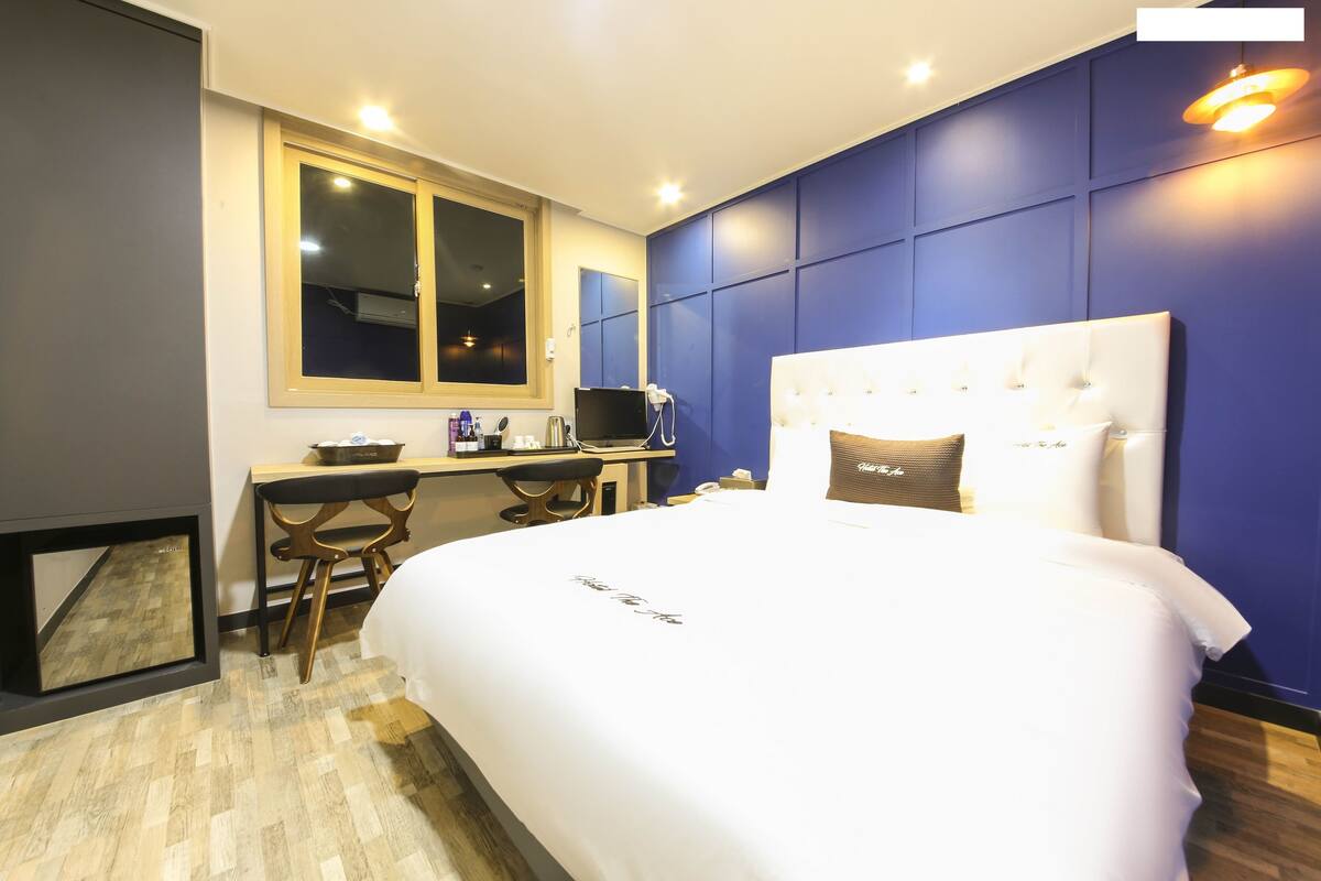 Quarto de hotel com uma cama grande, uma escrivaninha com computador e uma janela.