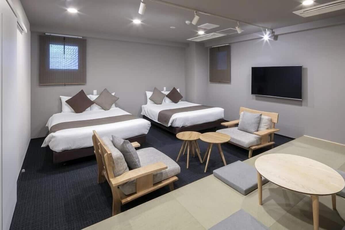 Quarto de hotel com duas camas, televisão, escrivaninha e área de estar com mesa redonda e cadeiras.