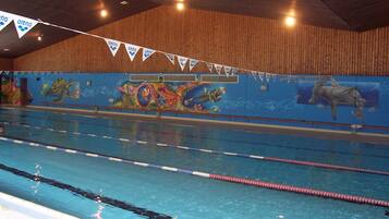 Piscina interior com divisórias de pista, paredes de painel de madeira e um mural retratando vida marinha.