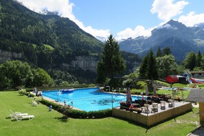 Piscina com área de deck, cercada por paisagem verdejante e montanhas ao fundo.