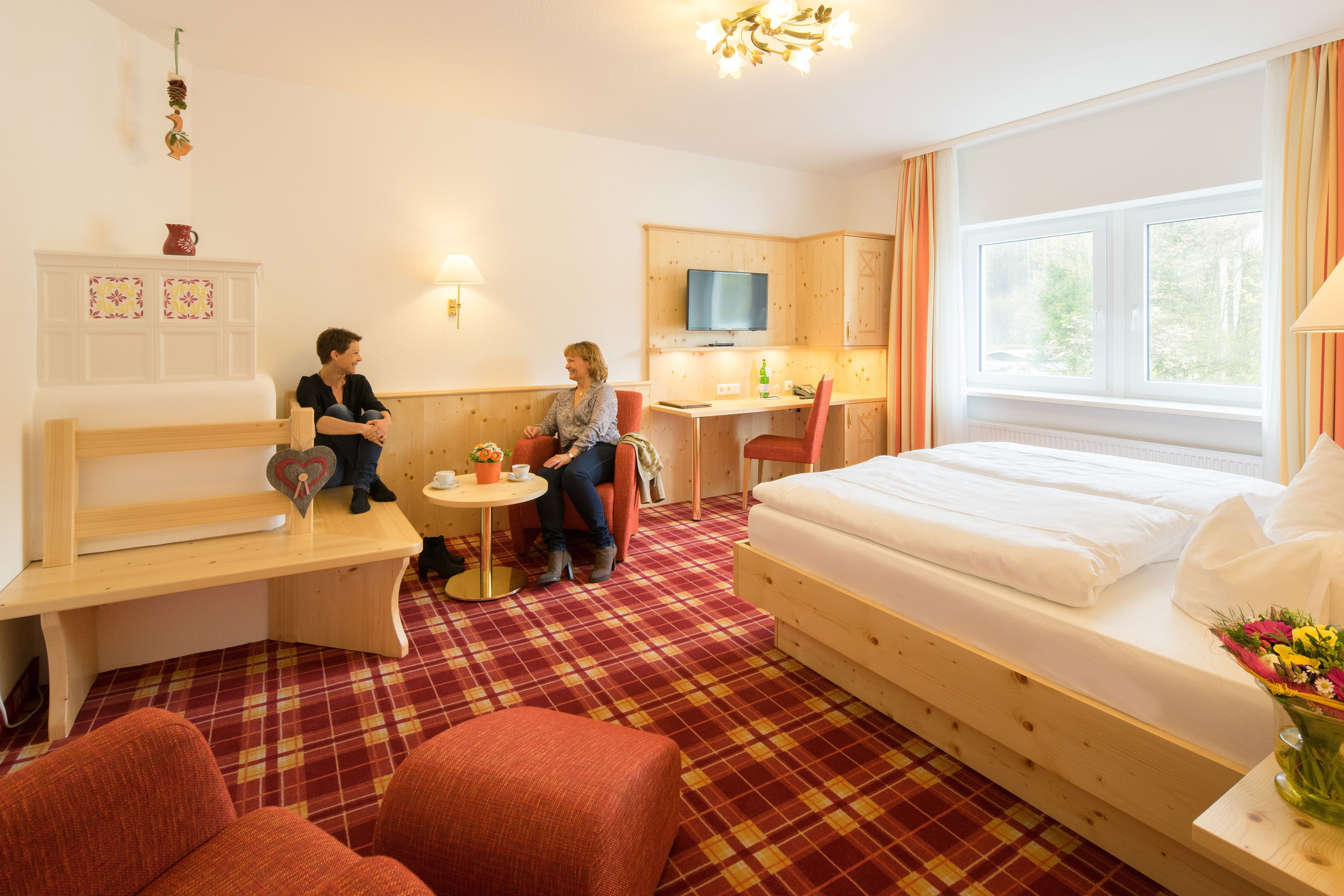 Quarto de hotel com cama, escrivaninha, televisão e área de estar com duas cadeiras e uma mesa.