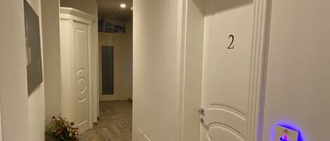 Um corredor com piso de madeira, paredes brancas e portas numeradas 2 e 3.