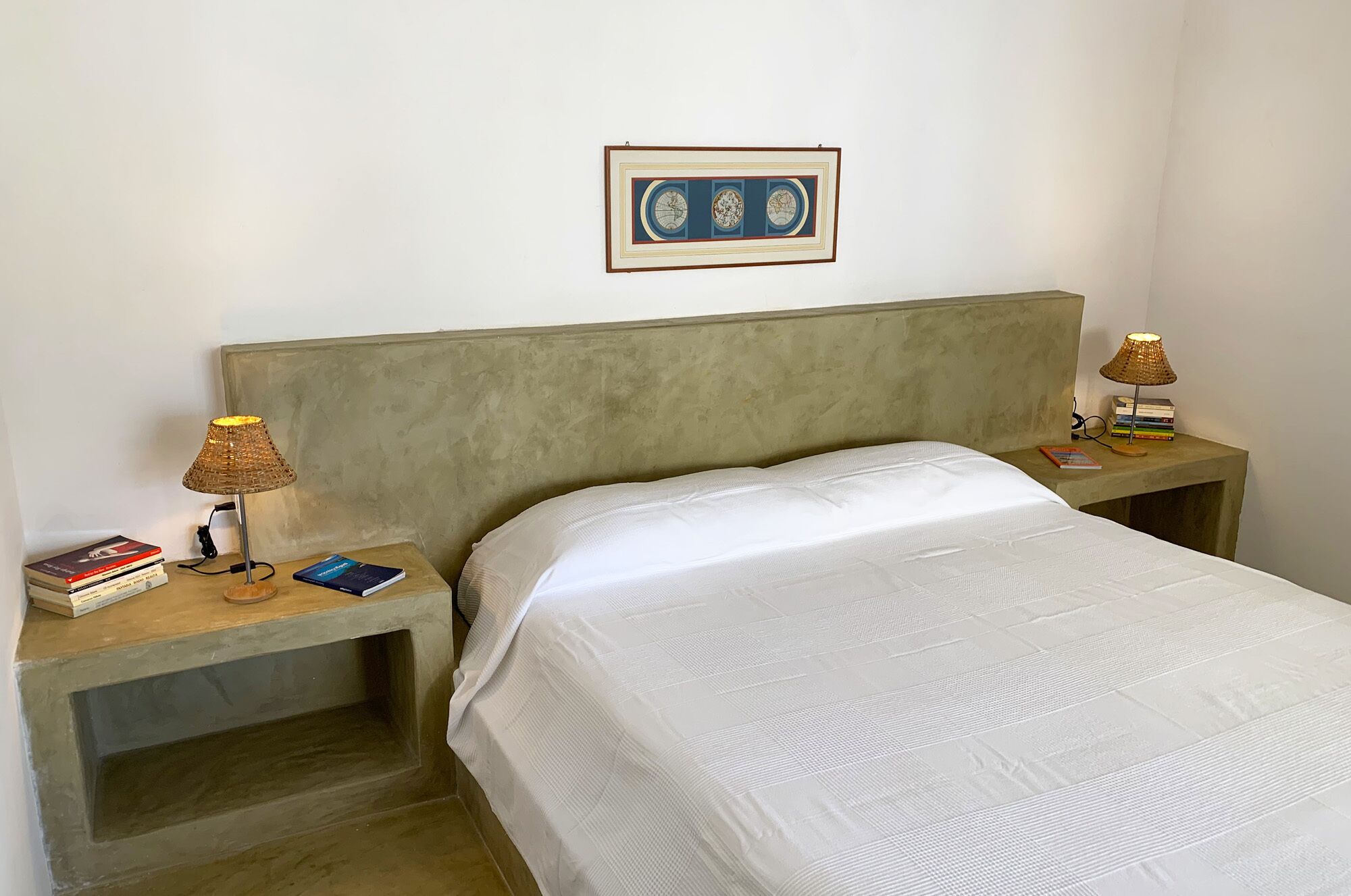 Quarto com cama, duas mesas de cabeceira, abajur e um quadro na parede.