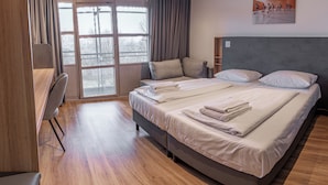 Quarto de hotel moderno com uma cama grande, uma escrivaninha e vista para o exterior.