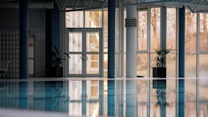 Piscina com reflexos nítidos, amplas janelas e plantas em vasos.