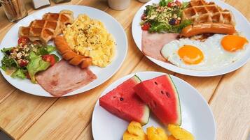 Uma mesa com três pratos de comida, incluindo waffles, ovos, presunto e uma salada.
