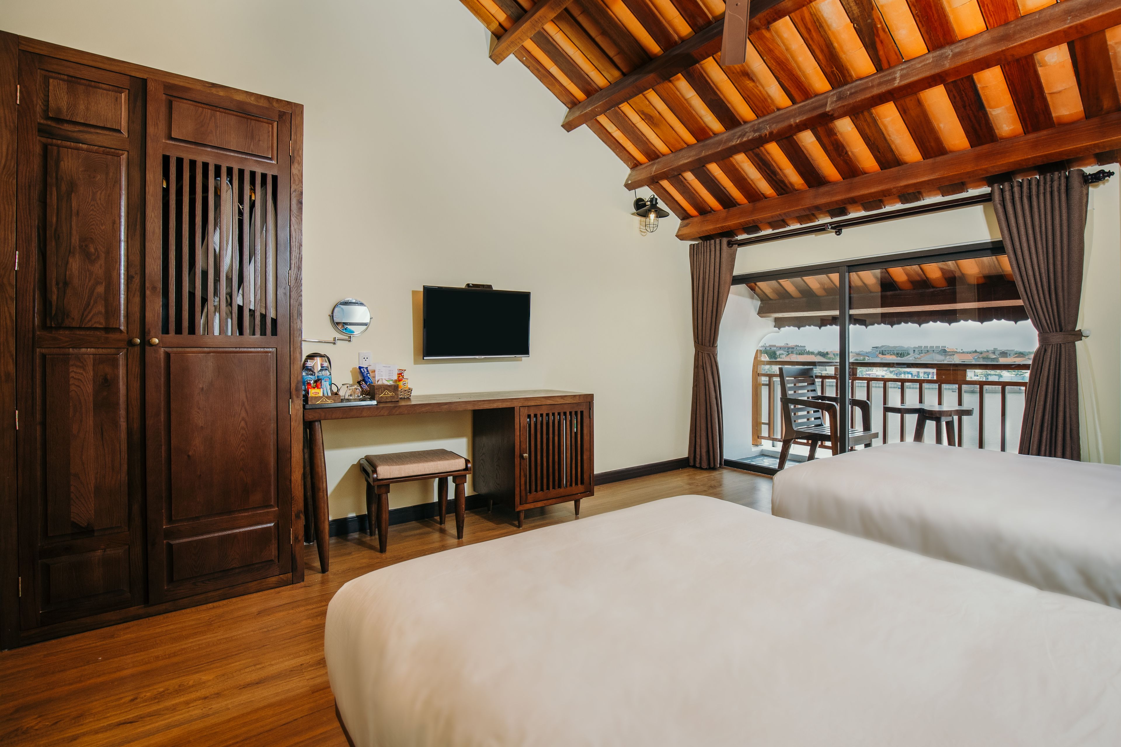 Quarto de hotel com duas camas, uma escrivaninha com cadeira, televisão e varanda com vista.