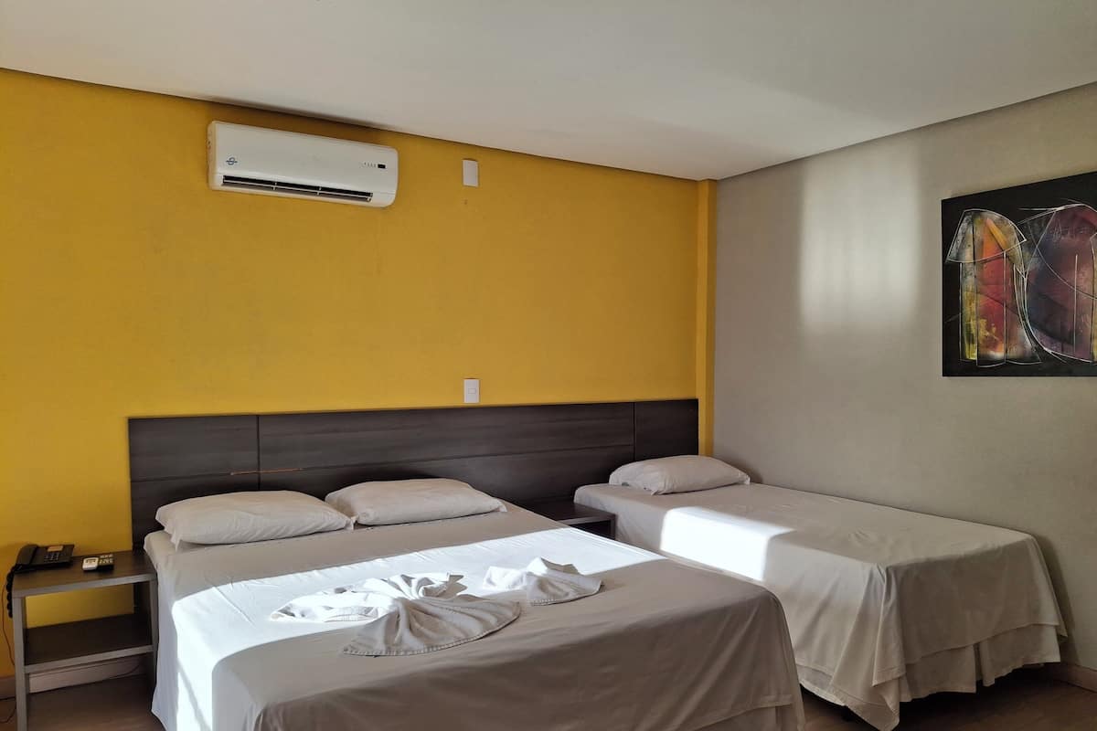 Quarto de hotel com duas camas, uma mesinha de cabeceira, ar condicionado e um quadro na parede.