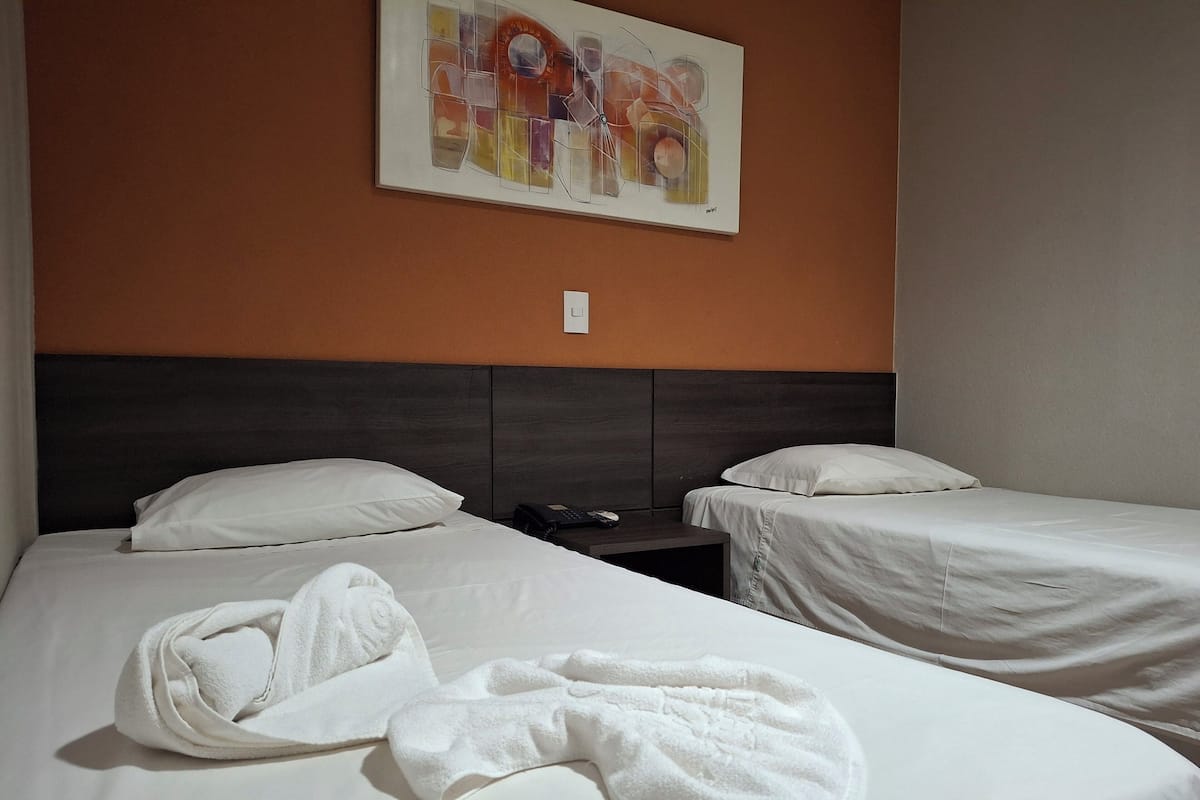 Quarto de hotel com duas camas, um quadro na parede e um telefone no criado-mudo.
