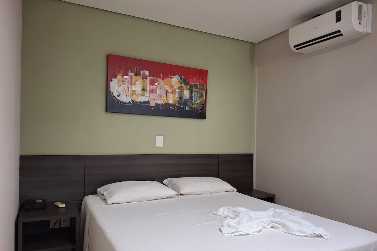 Quarto de hotel com cama, mesa de cabeceira, ar condicionado e um quadro na parede.