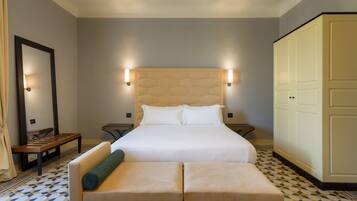 Quarto de hotel com uma cama grande, uma mesa de cabeceira, um banco, um guarda-roupa e um chão estampado.