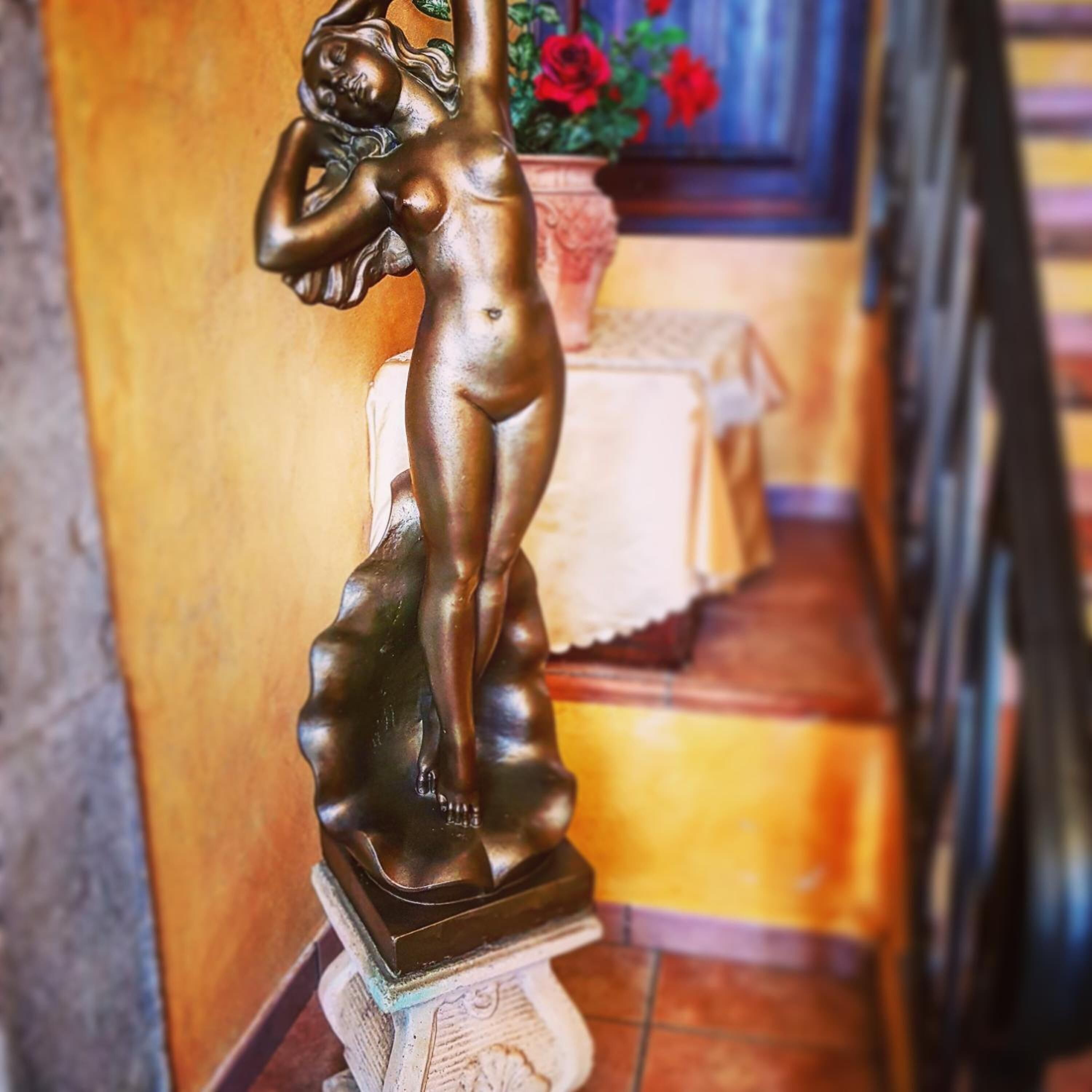 Estátua de bronze de uma mulher em pose dinâmica, sobre um pedestal.