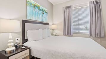 Quarto de hotel com uma cama grande, mesa de cabeceira com abajur, um quadro na parede e uma janela com cortinas.