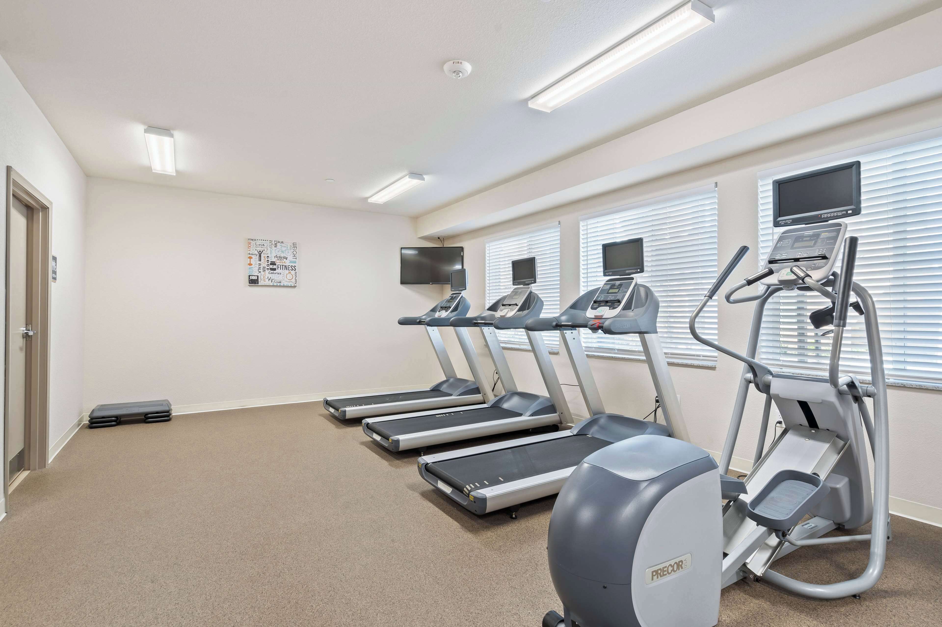 Sala de ginástica com esteiras, elíptico e bicicleta ergométrica.