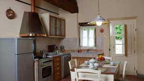 Uma cozinha com fogão, forno e pia, armários de madeira e uma mesa de jantar com cadeiras.
