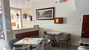 Uma área de refeições moderna com mesa de vidro, cadeiras estofadas cinzas, parede de pedra com quadro enquadrado e porta vermelha.