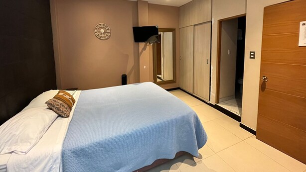 Quarto com cama, guarda-roupa, espelho e relógio na parede.