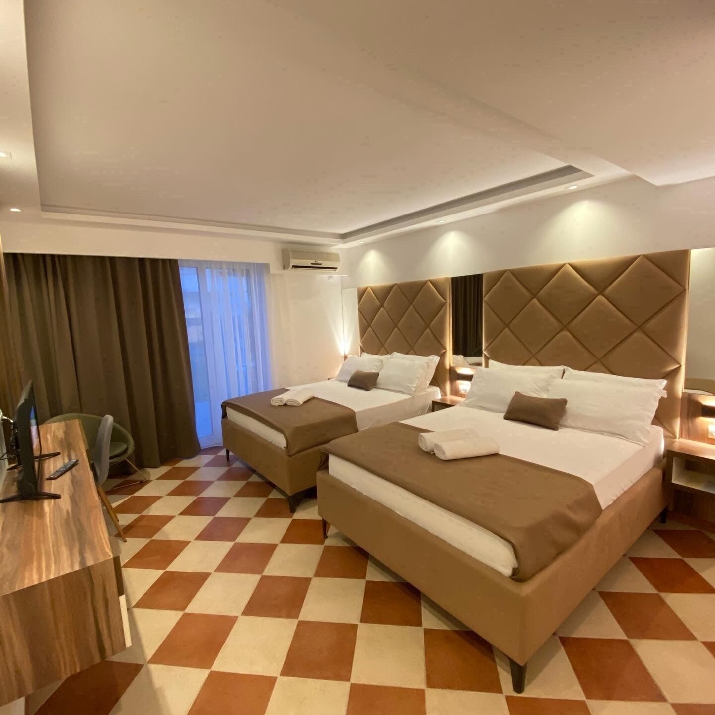 Quarto de hotel com duas camas, uma escrivaninha e uma cadeira.