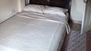 Uma cama de solteiro com cabeceira escura em um quarto com paredes lisas e um tapete estampado.
