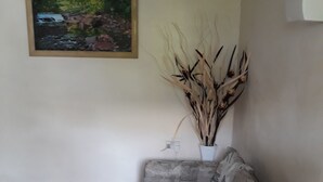 Uma sala de estar com um sofá estampado, um quadro na parede e um vaso com plantas secas.
