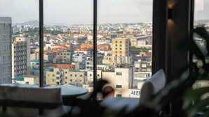 Vista da janela sobre um horizonte urbano com edifícios e uma montanha ao longe.