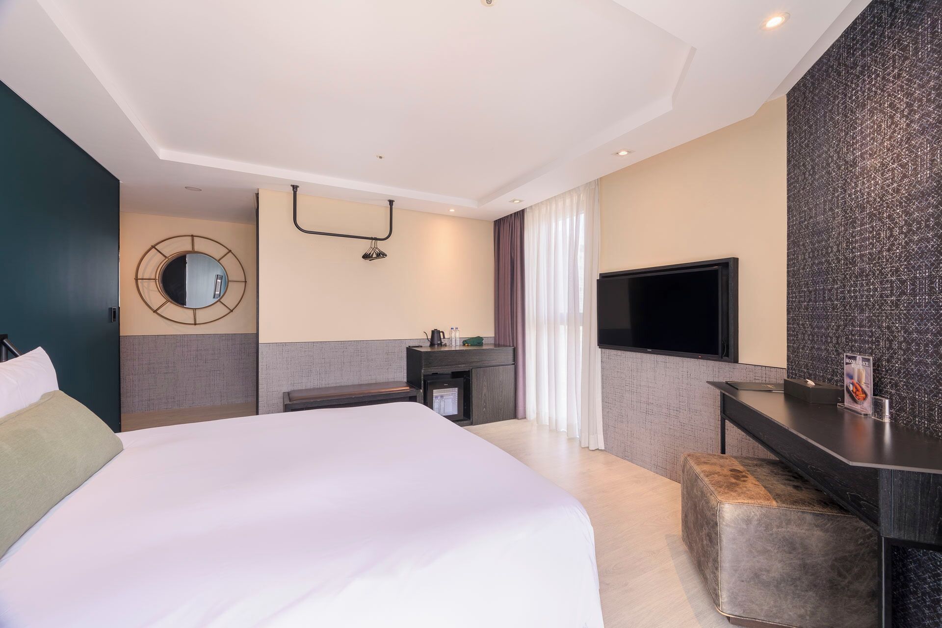 Quarto de hotel com uma cama grande, uma escrivaninha, televisão de tela plana, espelho e janela com cortinas.
