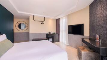 Quarto de hotel com uma cama grande, uma escrivaninha, televisão de tela plana, espelho e janela com cortinas.