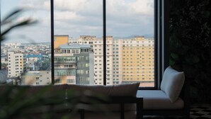 Quarto com uma janela ampla que oferece vista para a cidade, piso xadrez e um sofá branco.