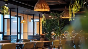 Interior de restaurante com mesas, cadeiras, luminárias pendentes e janelas amplas.