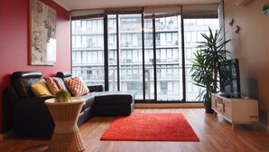 Sala de estar moderna com sofá preto, tapete vermelho e uma grande janela com vista para a cidade.