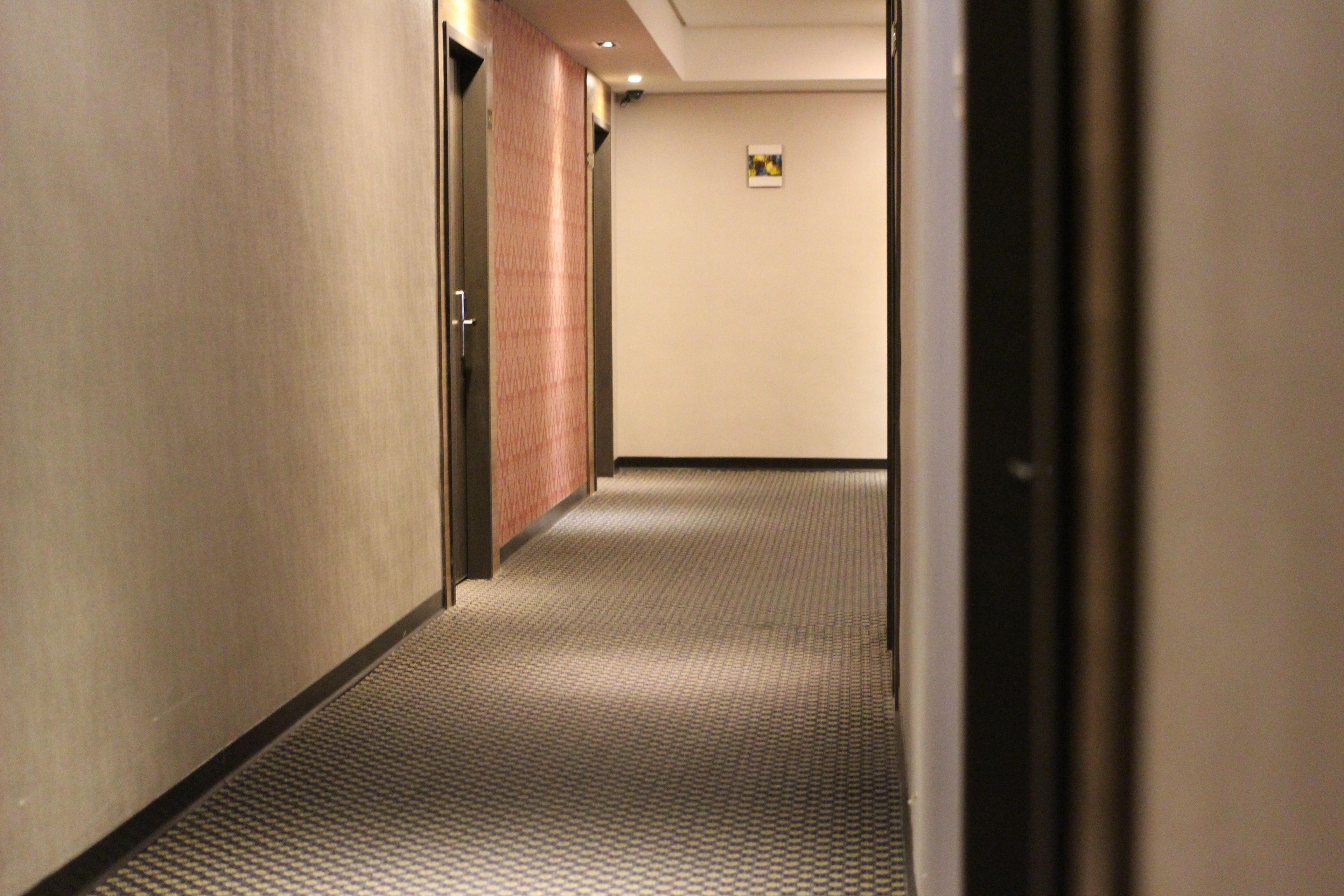 Um corredor com piso carpetado, uma porta à esquerda e uma parede com um pequeno quadro.