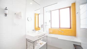 Uma casa de banho moderna com uma pia branca, um espelho, uma cabine de duche e uma janela com uma parede de tijolos amarelos.