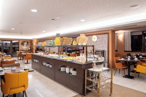 Uma área de buffet com diversos alimentos, um espaço de estar com cadeiras laranja e um balcão com um caixa registradora.