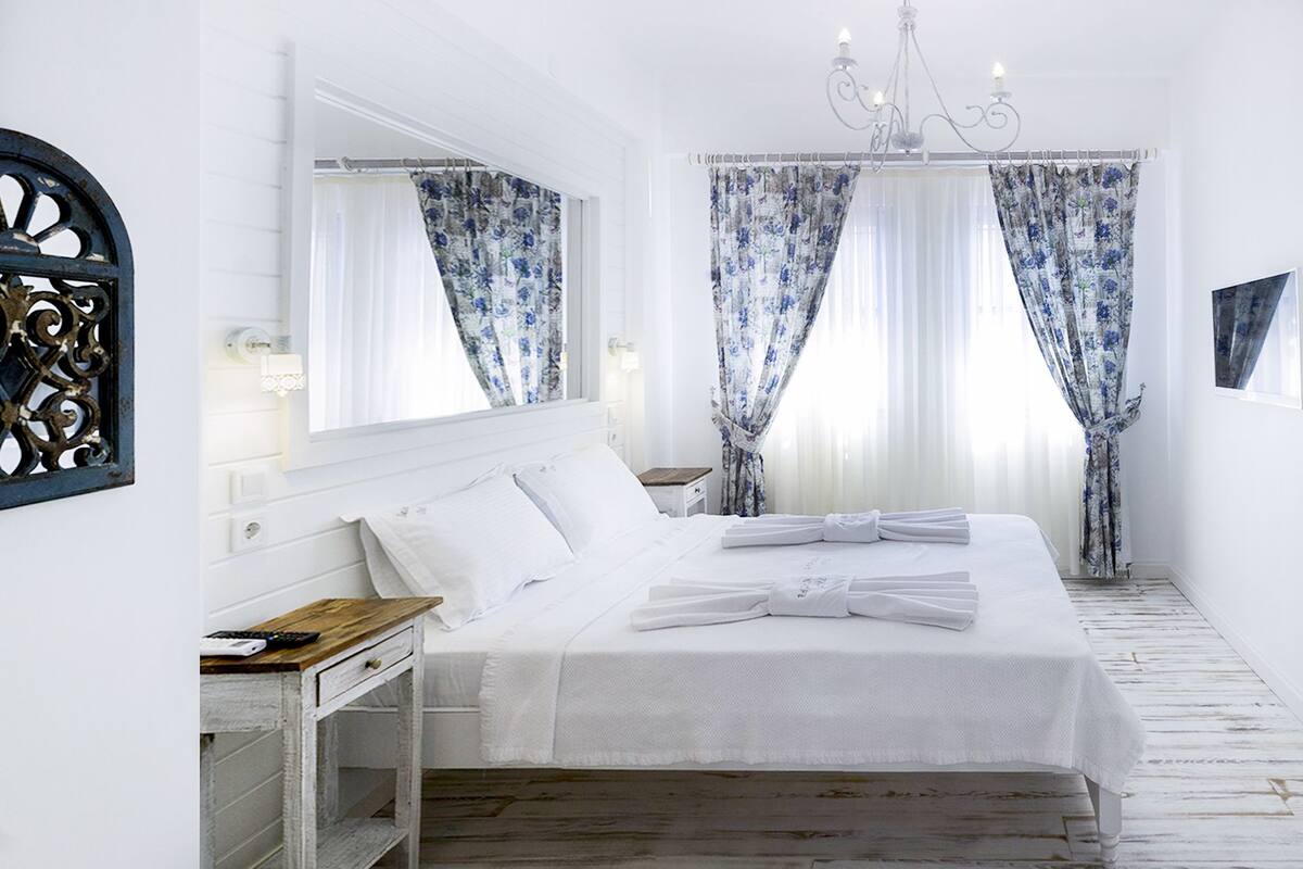 Quarto com cama, mesa de cabeceira, piso de madeira e lustre.