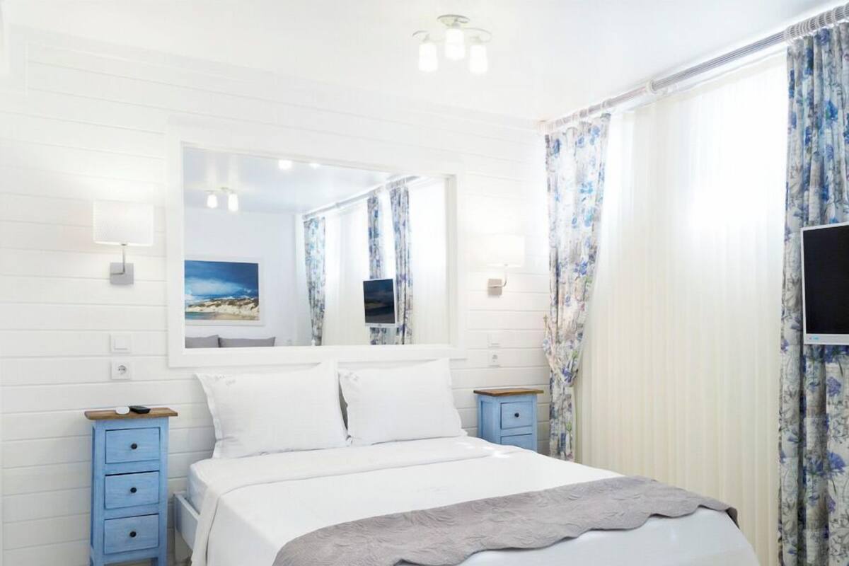 Quarto com uma cama grande, duas mesas de cabeceira, cômoda, espelho e televisão.
