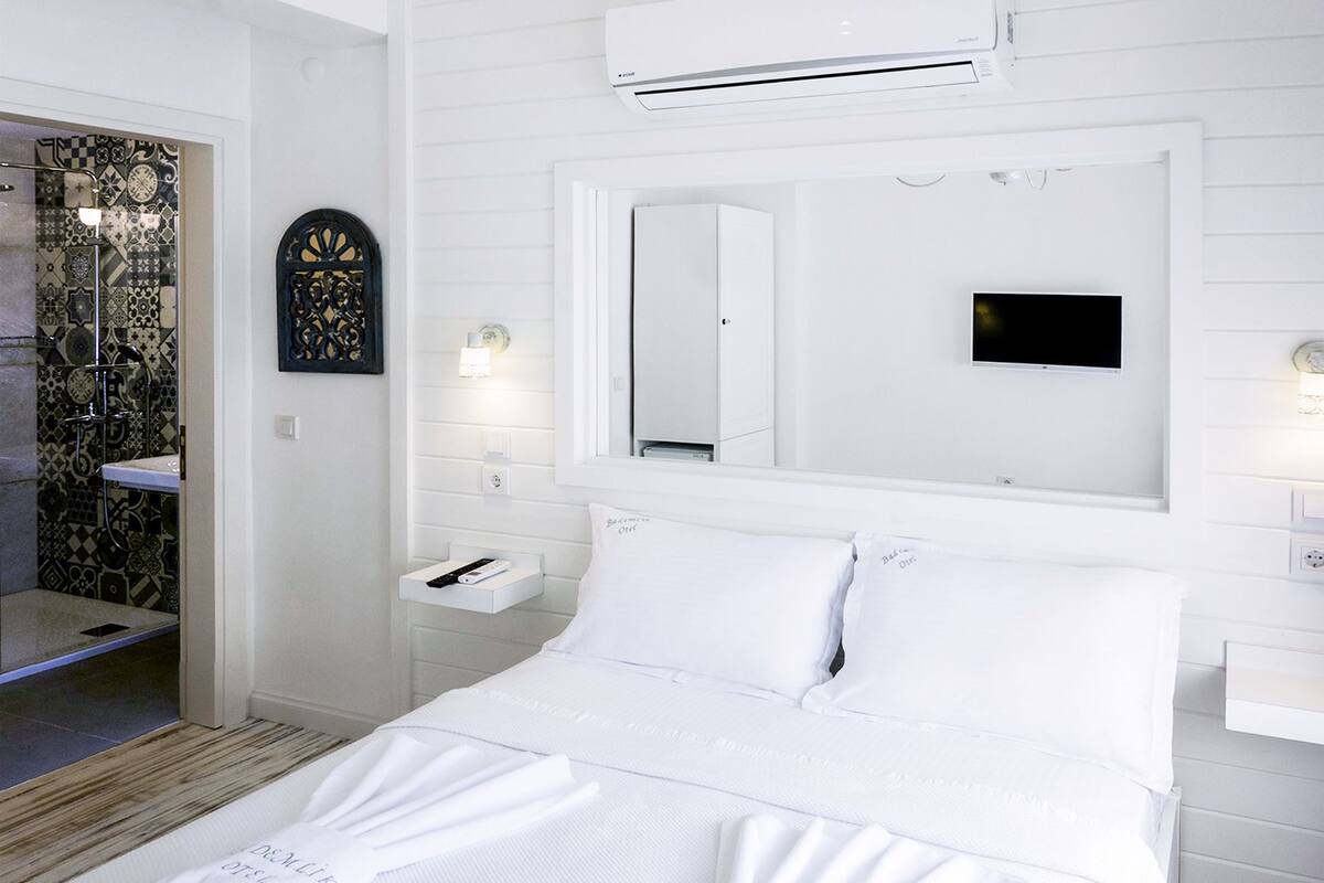 Quarto de hotel com cama, mesa de cabeceira, espelho e aparelho de ar condicionado.