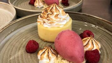 Sobremesa com cheesecake coberto de merengue e framboesas em um prato de cerâmica.