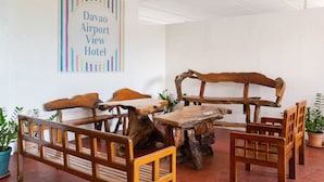 Quarto com mobiliário de madeira rústica, incluindo um banco e cadeiras, e uma placa na parede com a inscrição "Davao Airport View Hotel".