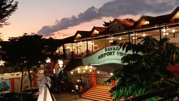 Exterior do Terminal do Aeroporto de Davao, com uma escadaria que leva à entrada, rodeado por vegetação e um céu ao pôr do sol.