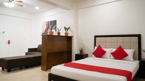 Quarto de hotel com uma cama, área de estar, um armário de madeira e um ventilador de teto.